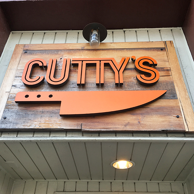 Cutty's simple wooden sign with that iconic orange knife logo &ndash; like a secret handshake for sandwich aficionados who know what awaits inside.