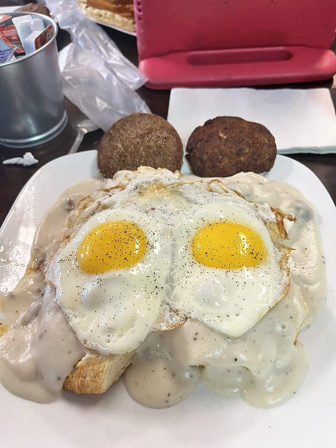 Two sunny-side up eggs gazing optimistically at you from their creamy gravy pond, with sausage patties standing guard like delicious sentinels.