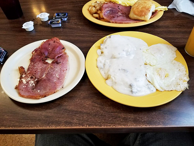 The holy trinity of country breakfast: ham with that perfect pink hue, eggs cooked just right, and biscuits swimming in pepper-flecked gravy.