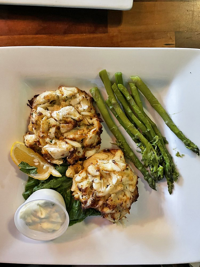 Two golden-brown crab cakes nestled beside vibrant asparagus spears&mdash;proof that sometimes the simplest presentations deliver the most profound flavors.