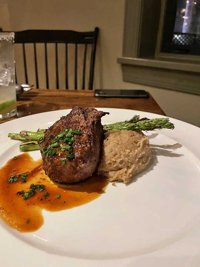 The filet mignon arrives like royalty, perched atop a throne of mashed potatoes with asparagus courtiers and a sauce that demands to be savored.