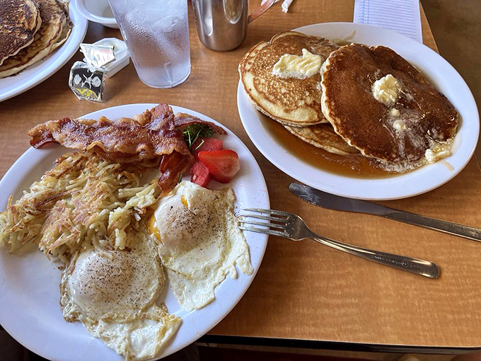 Breakfast nirvana achieved: golden pancakes bathed in syrup alongside perfectly fried eggs and crispy hash browns. Morning glory on a plate.
