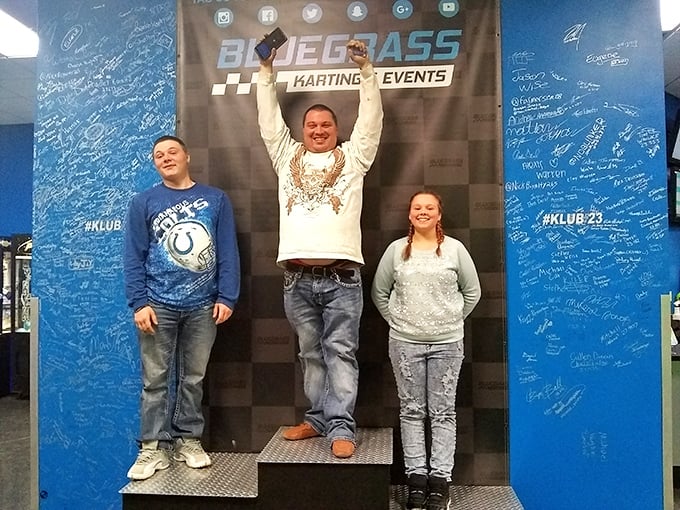 Every champion needs their moment on the podium. The blue wall behind them holds the signatures of countless weekend warriors.