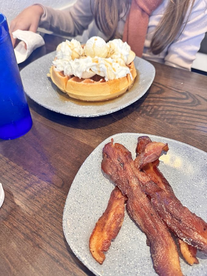 A waffle topped with whipped cream and ice cream alongside perfectly crisped bacon &ndash; breakfast and dessert having a delicious identity crisis.