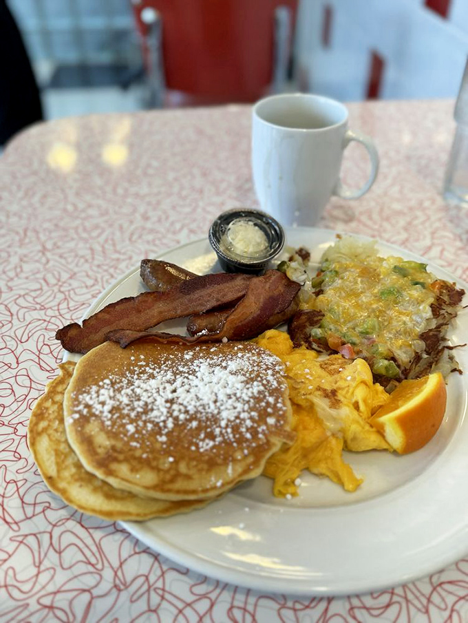 The holy trinity of breakfast perfection: golden pancakes dusted with powdered sugar, eggs scrambled to fluffy perfection, and bacon that's achieved that magical crisp-yet-chewy state.