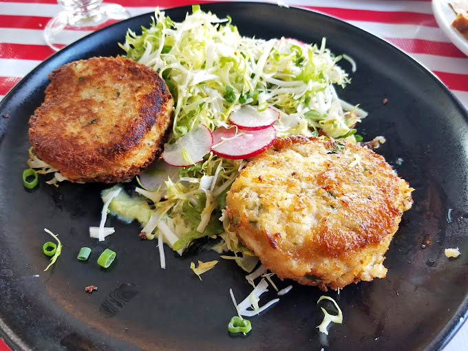 Two perfect crab cakes on a black slate canvas&mdash;like seafood performance art. That golden crust keeps secrets only your taste buds will discover.