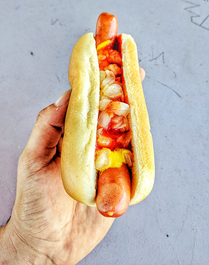 The classic hot dog with all the fixings&mdash;proof that perfection doesn't need to be complicated. Just mustard, ketchup, onions, and happiness.