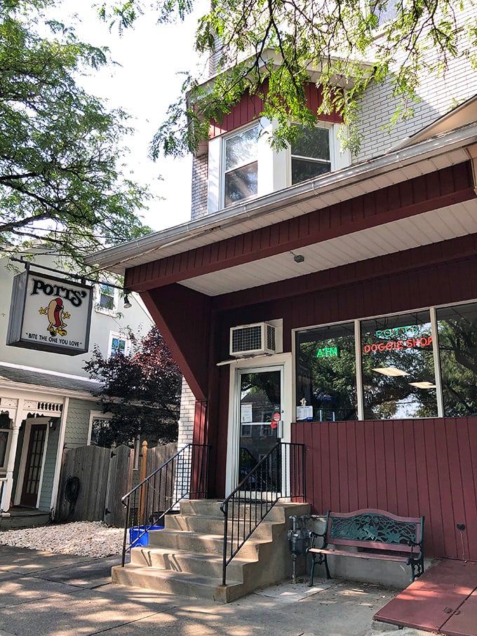 The cozy red storefront of Potts' Doggie Shop offers a warm welcome. That bench outside has witnessed countless hot dog happiness moments. 