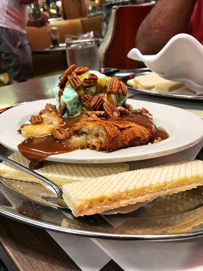 This isn't just dessert - it's architecture. A foundation of warm apple cobbler supporting towers of pecans and that famous hot fudge river.