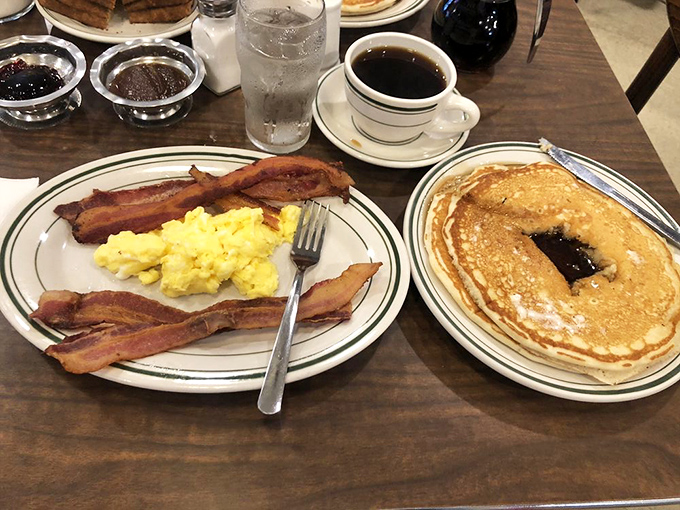 Breakfast's perfect trinity: crispy bacon, fluffy scrambled eggs, and pancakes waiting patiently for their maple baptism.