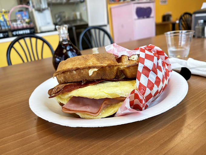 Breakfast sandwich perfection: eggs, ham, and cheese nestled between golden waffle "bread." The red checkered paper says "diner classic," but your taste buds say "revelation."