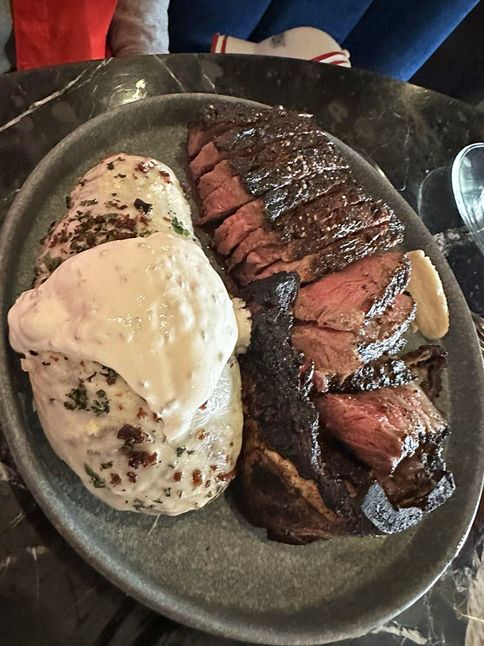 A baked potato cozying up to a Kansas City Strip that's been kissed by flame and seasoned by someone who clearly respects the art of beef.