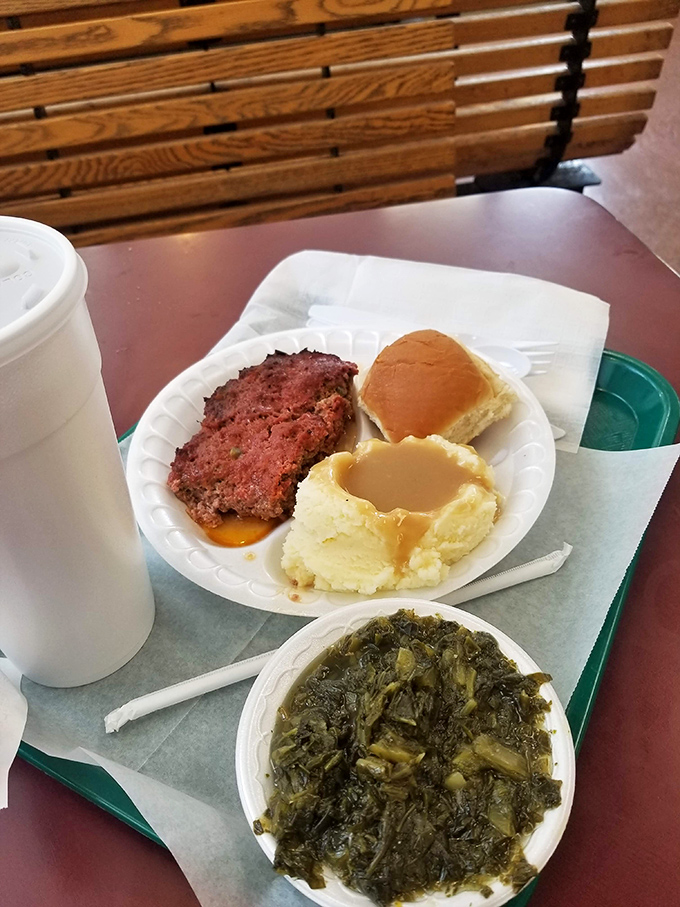 Meatloaf, mashed potatoes bathed in gravy, and collard greens—the holy trinity of Southern comfort food served on unpretentious paper plates.