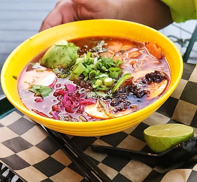 Ramen meets birria in this cross-cultural masterpiece. The bright yellow bowl cradles a broth so rich it could buy a vacation home.