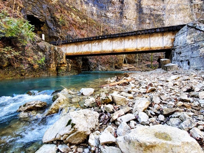 Where rushing water meets industrial history, Stock Creek flows beneath rusted railroad infrastructure in a timeline-bending tableau.