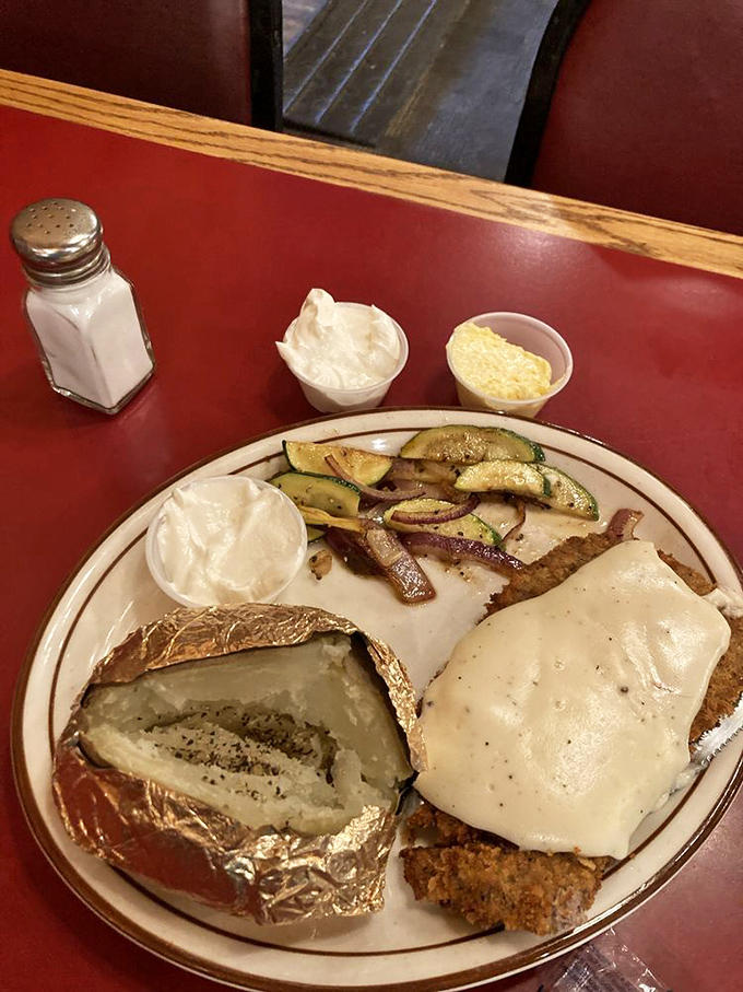 The burger arrives like a cheesy crown atop its throne, with onion rings standing guard and fresh veggies providing a token nod to nutrition. 