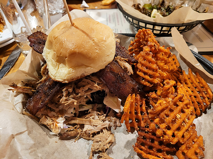 A sandwich that requires both hands and a strategy. Sweet potato waffle fries stand guard, knowing they'll soon be drafted into sauce-mopping duty. 