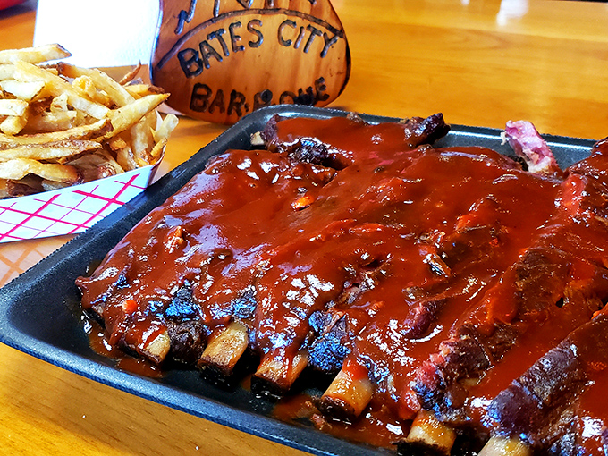 A rack of ribs lounging in sauce like it's taking a flavor bath, with coleslaw and fries standing by as willing accomplices.