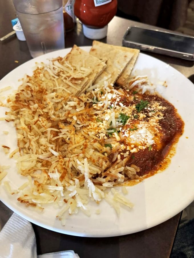 Hearty breakfast meets global inspiration with this savory dish featuring eggs nestled in tangy sauce, paired with crispy hashbrowns and warm tortillas.