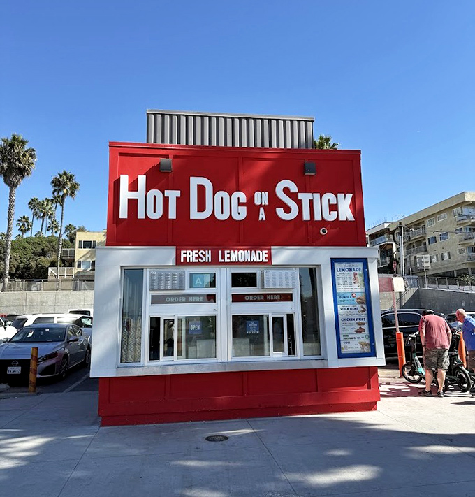 Hot Dog on a Stick's bold red stand against the California sky &ndash; a beacon of fried perfection that's outlasted countless food trends.