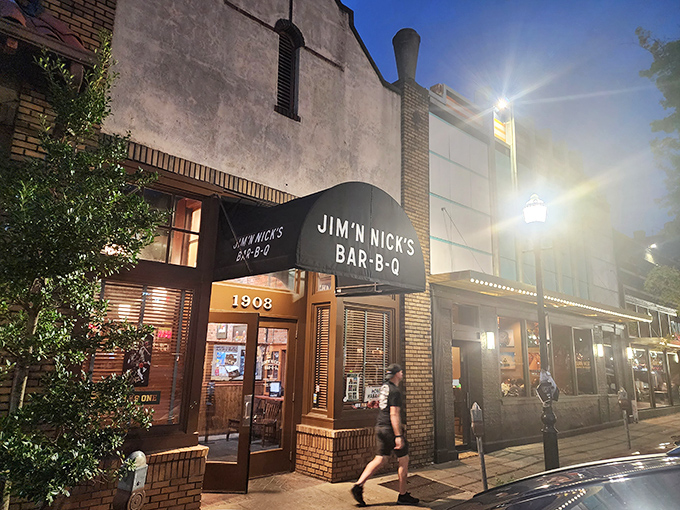Jim 'N Nick's evening glow feels like a BBQ welcome committee. That brick facade hides a wood-fired wonderland of smoky treasures.