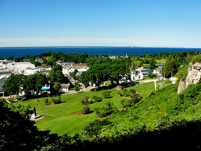 From Mackinac's heights, the island unfolds below like a lush green carpet rolling toward endless blue waters.