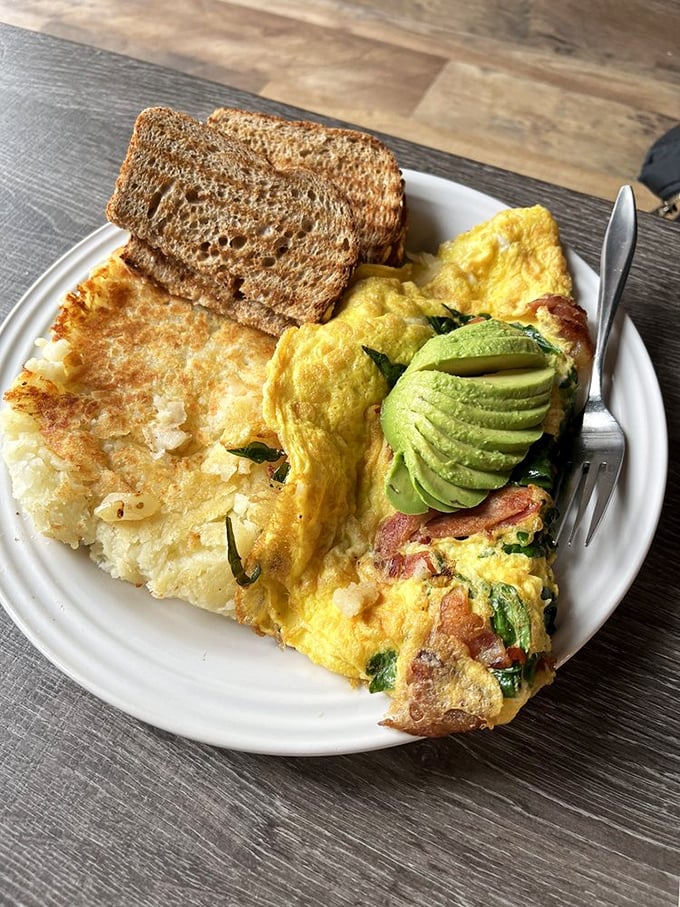 Breakfast nirvana achieved: a fluffy omelet studded with avocado and bacon, paired with perfectly crispy home fries and toast. Morning glory on a plate.