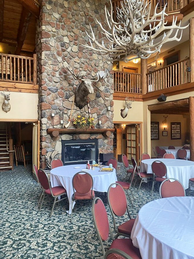 Morning light filters through towering windows while the imposing fireplace stands ready to warm both body and conversation around white-clothed tables.