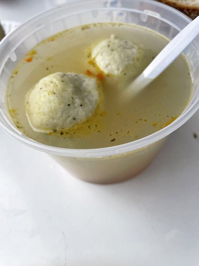 The holy trinity of deli comfort: matzo ball soup, a towering sandwich, and a proper pickle. Happiness served on disposable dishware.