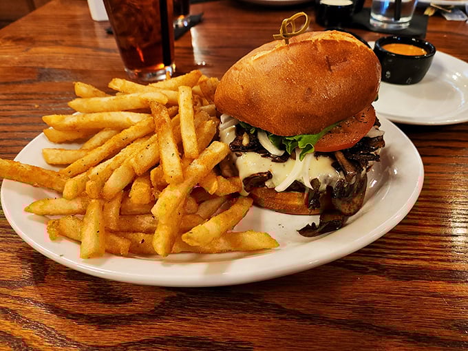 Your savory burger piled high with mushrooms and Swiss cheese sits alongside a mountain of golden, crispy fries for you.
