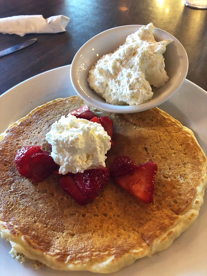 The pancakes wear their strawberries and cream like jewelry, but the real star is that cloud of whipped goodness performing a magic trick on the side.
