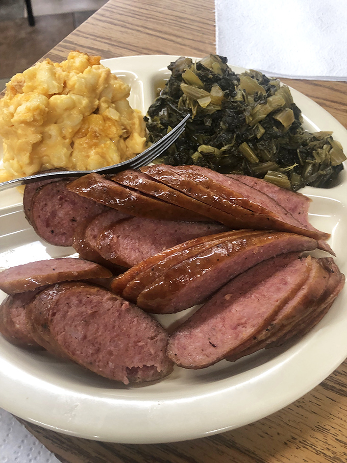 Sausage sliced with precision alongside mac and cheese and greens. This plate isn't just lunch&mdash;it's a Southern symphony on porcelain.