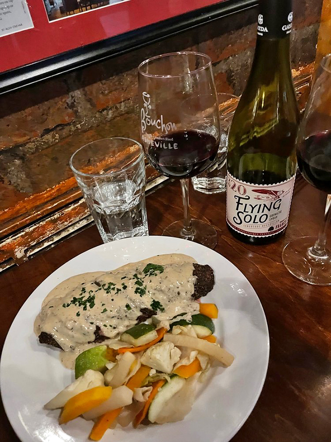 Steak bathed in peppercorn sauce alongside fresh vegetables, with wine standing by to complete civilization's perfect trifecta.