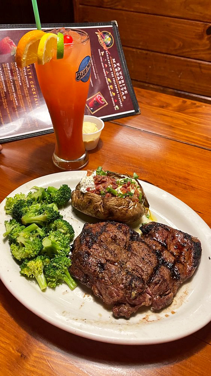 The holy trinity of dining pleasure: a perfectly cooked steak, a loaded baked potato, and a colorful cocktail that says "vacation mode activated."