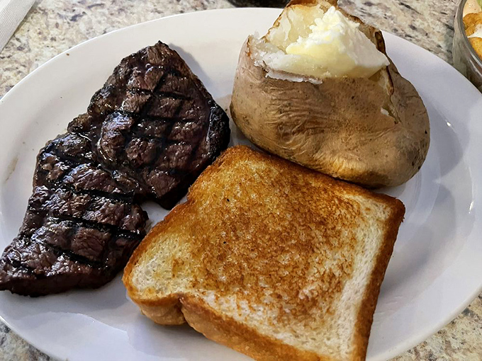 The holy trinity of steakhouse perfection: a perfectly grilled cut, a fluffy baked potato bursting with butter, and toast to soak up every precious drop.