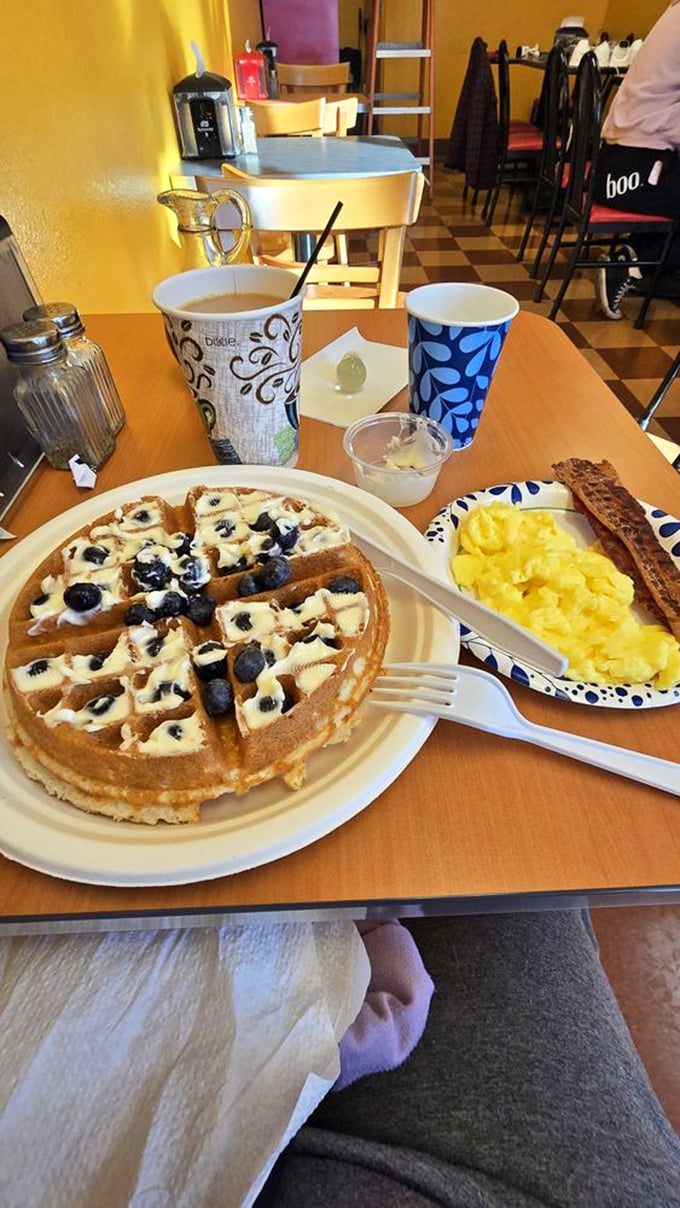 A blueberry-studded waffle with scrambled eggs and bacon on the side—proof that balance in the universe is possible, at least on your breakfast plate.