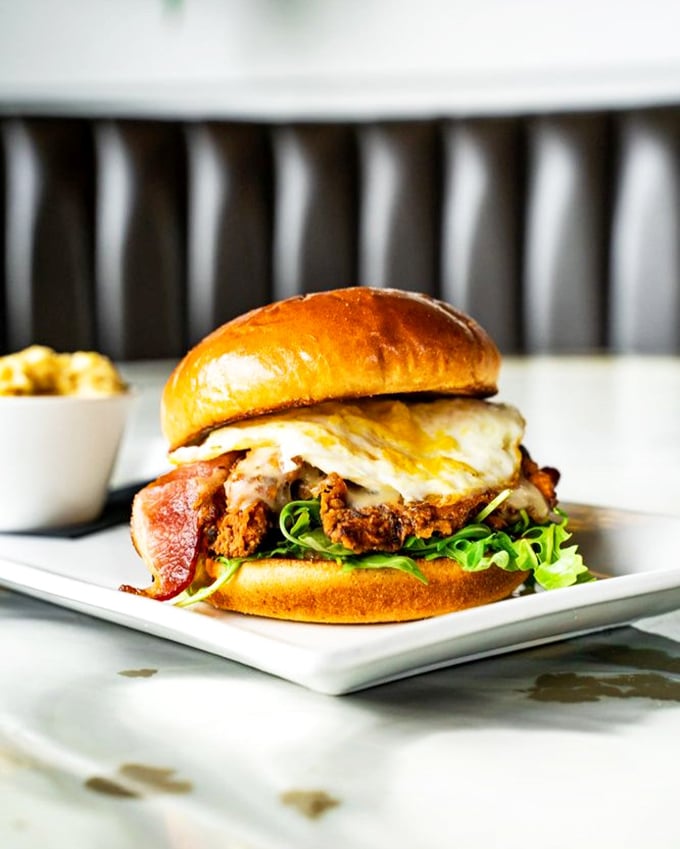 This isn't just a burger, it's a tower of morning glory &ndash; fried chicken, bacon, egg, and greens stacked higher than your weekend expectations.