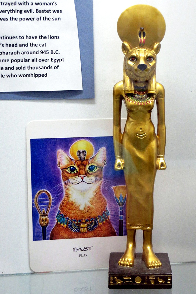 The golden statue of Bastet stands regally beside her modern counterpart, spanning 3,000 years of humans thinking, "Yes, cats ARE divine."