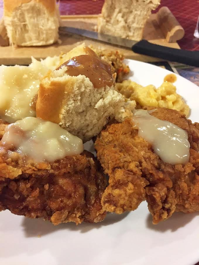 Fried chicken so golden it deserves its own trophy, nestled beside mashed potatoes and homemade rolls. This plate is why elastic waistbands were invented.