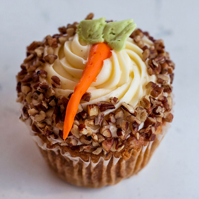 A carrot cake cupcake with personality&mdash;cream cheese frosting swirled like a cloud, nuts for crunch, and that cute carrot garnish saying "yes, eat me."