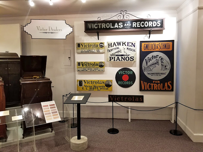 A wall of vintage advertisements reveals how Victor marketed their machines &ndash; not just as technology, but as furniture worthy of your finest room.