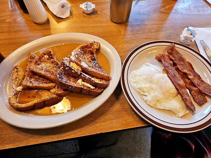 French toast so golden it belongs in Fort Knox. Drowning in syrup with bacon standing guard&mdash;breakfast doesn't get more American than this.