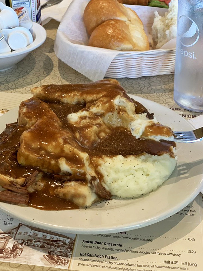 Comfort food incarnate: tender roast beef swimming in rich gravy atop cloud-like mashed potatoes. The bread basket in the background is plotting your delicious downfall.