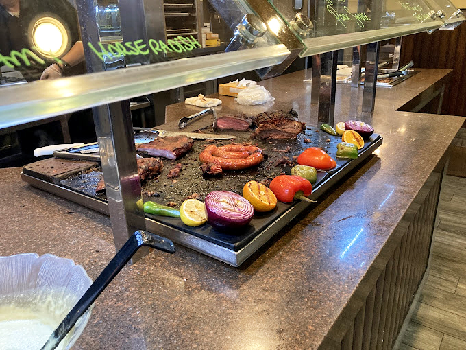 The carving station—where meat meets heat meets your eager plate. Those grilled vegetables are just there to ease your conscience.
