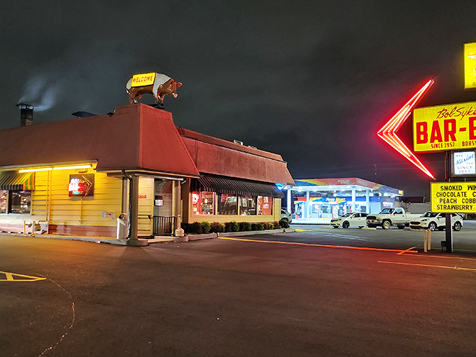 Bob Sykes' neon arrow cuts through the night like a BBQ lighthouse, guiding hungry travelers to pork paradise since before GPS was a thing.