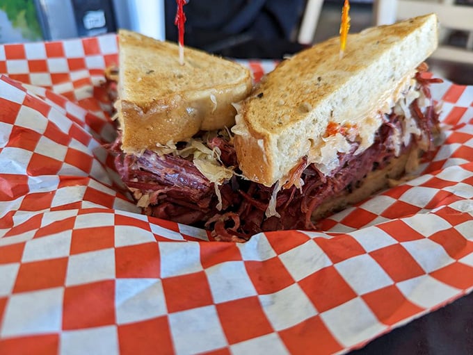 The classic Reuben in its natural habitat—checkered paper, pickle companion, and the anticipation of that first perfect bite. Poetry on a plate.