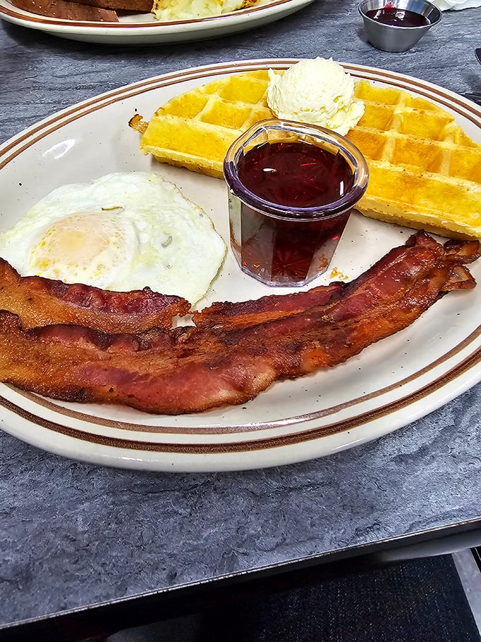 The breakfast trinity: crispy bacon, sunny-side-up egg, and golden waffle. Like a morning symphony where every instrument plays its part perfectly.