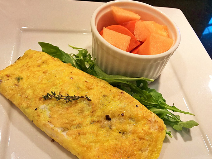 Breakfast perfection on a plate: A golden omelet nestled alongside fresh greens and sweet cantaloupe &ndash; simple, flawless execution to start your day.