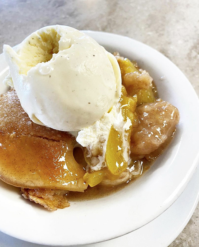 Peach cobbler crowned with ice cream melting into warm, cinnamon-spiced fruit—the kind of dessert that makes you seriously consider licking the plate.