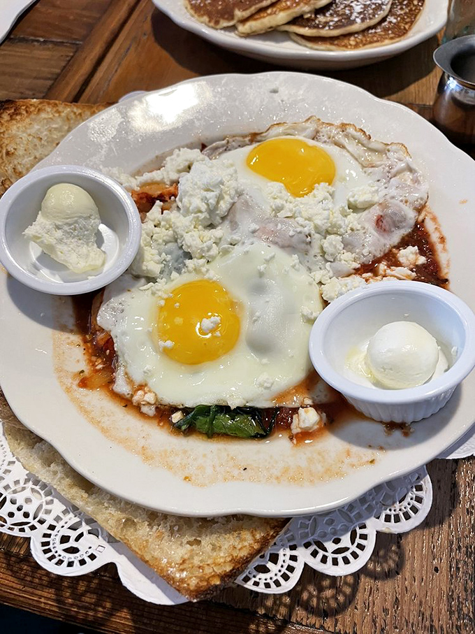 Two sunny-side eggs nestled in a savory bath with feta standing guard&mdash;proof that breakfast can be both sophisticated and deeply comforting.